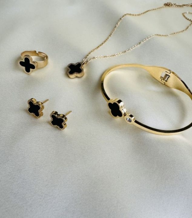The jewelry set is a luxurious gold-tone design with black clover ...